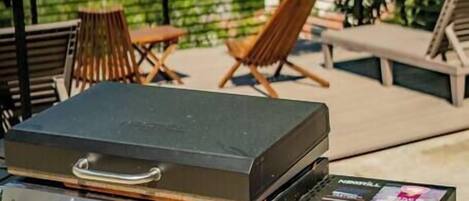 Uma churrasqueira NEXGRILL com carrinho, área de estar externa e vista para um lago.