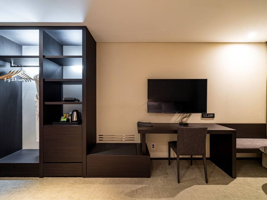 Quarto de hotel compacto com guarda-roupa embutido, secretária com cadeira, televisão de ecrã plano e um pequeno espaço de estar.