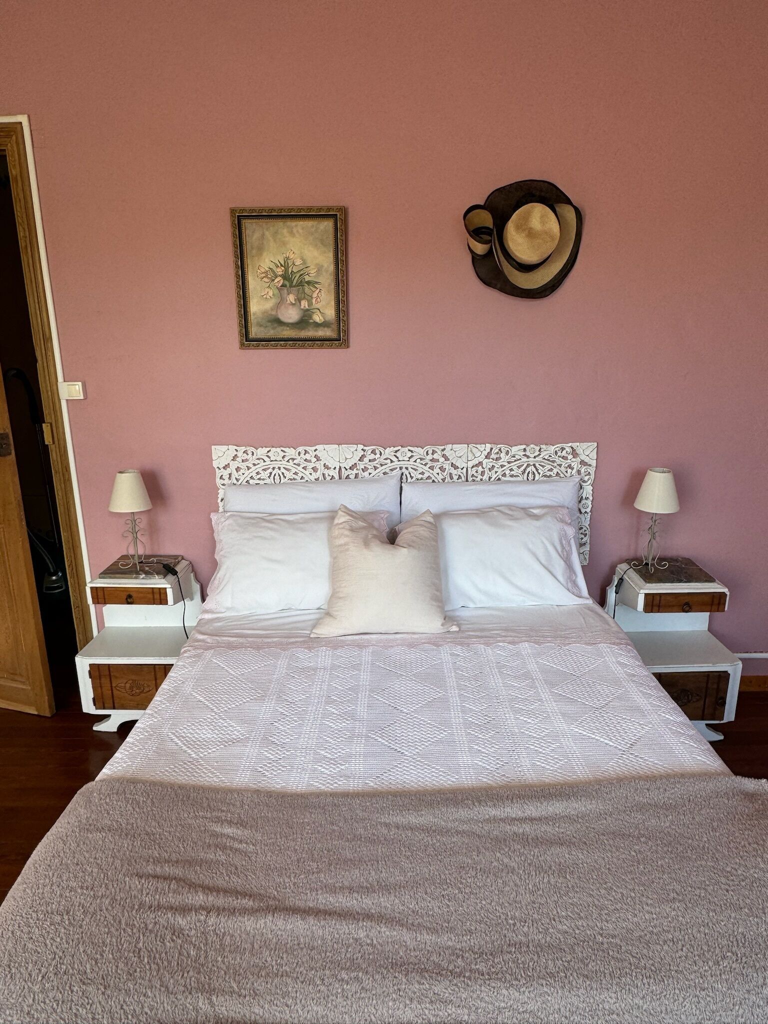 Quarto com uma cama, duas mesas de cabeceira, um criado-mudo e um chapéu pendurado na parede, além de um quadro emoldurado.