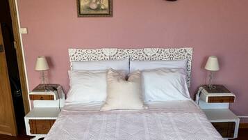 Quarto com uma cama, duas mesas de cabeceira, um criado-mudo e um chapéu pendurado na parede, além de um quadro emoldurado.