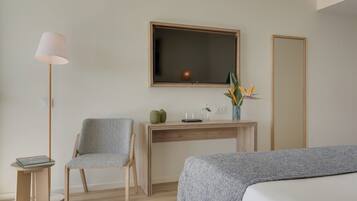 Quarto de hotel com uma cama, uma escrivaninha com um computador, uma cadeira, um abajur e um espelho.