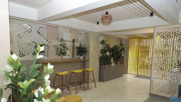 Decoração moderna com área de recepção, bar e assentos. Apresenta painéis decorativos, plantas e uma estátua.