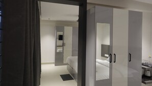 Quarto de hotel moderno com um guarda-roupa espaçoso, uma cama e uma pequena mesa de cabeceira com abajur.