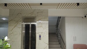 Um elevador moderno com paredes de mármore, uma escadaria com corrimãos de metal e uma almofada amarela em uma cadeira rosa.