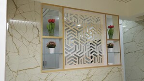 Um quarto com paredes de mármore, um separador decorativo com padrões geométricos e prateleiras com plantas em vasos.