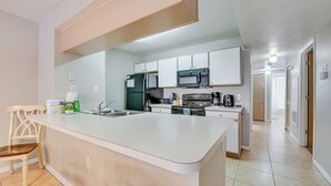Uma cozinha moderna com armários brancos, uma ilha central e um espaço de refeições com uma cadeira de madeira.