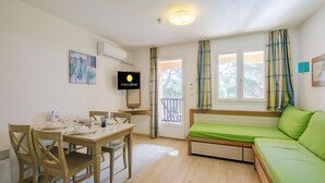 Um quarto com uma mesa de jantar, cadeiras, uma cama, uma televisão e uma janela com cortinas.