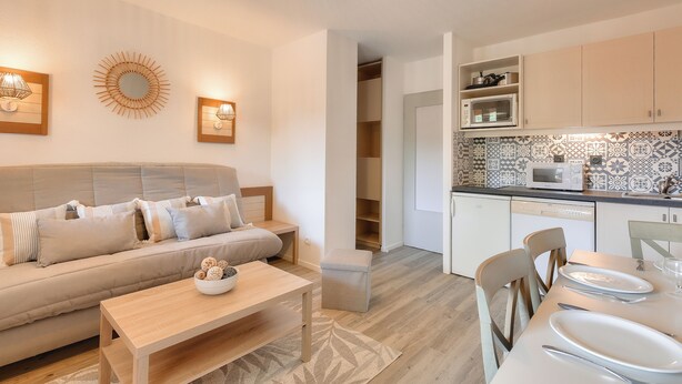 Uma sala de estar moderna com um sofá, uma mesa de centro e um espaço de jantar com cadeiras e uma mesa posta para dois.
