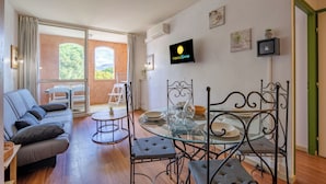 Uma sala de estar moderna com uma mesa de jantar de vidro, um sofá e uma TV fixada na parede.