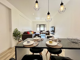 Uma sala de jantar moderna com uma mesa preta, jogos americanos trançados e cadeiras pretas.