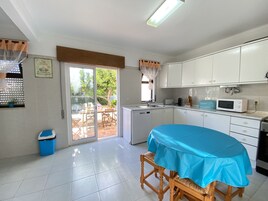 Cozinha com armários brancos, micro-ondas e mesa coberta por toalha azul.