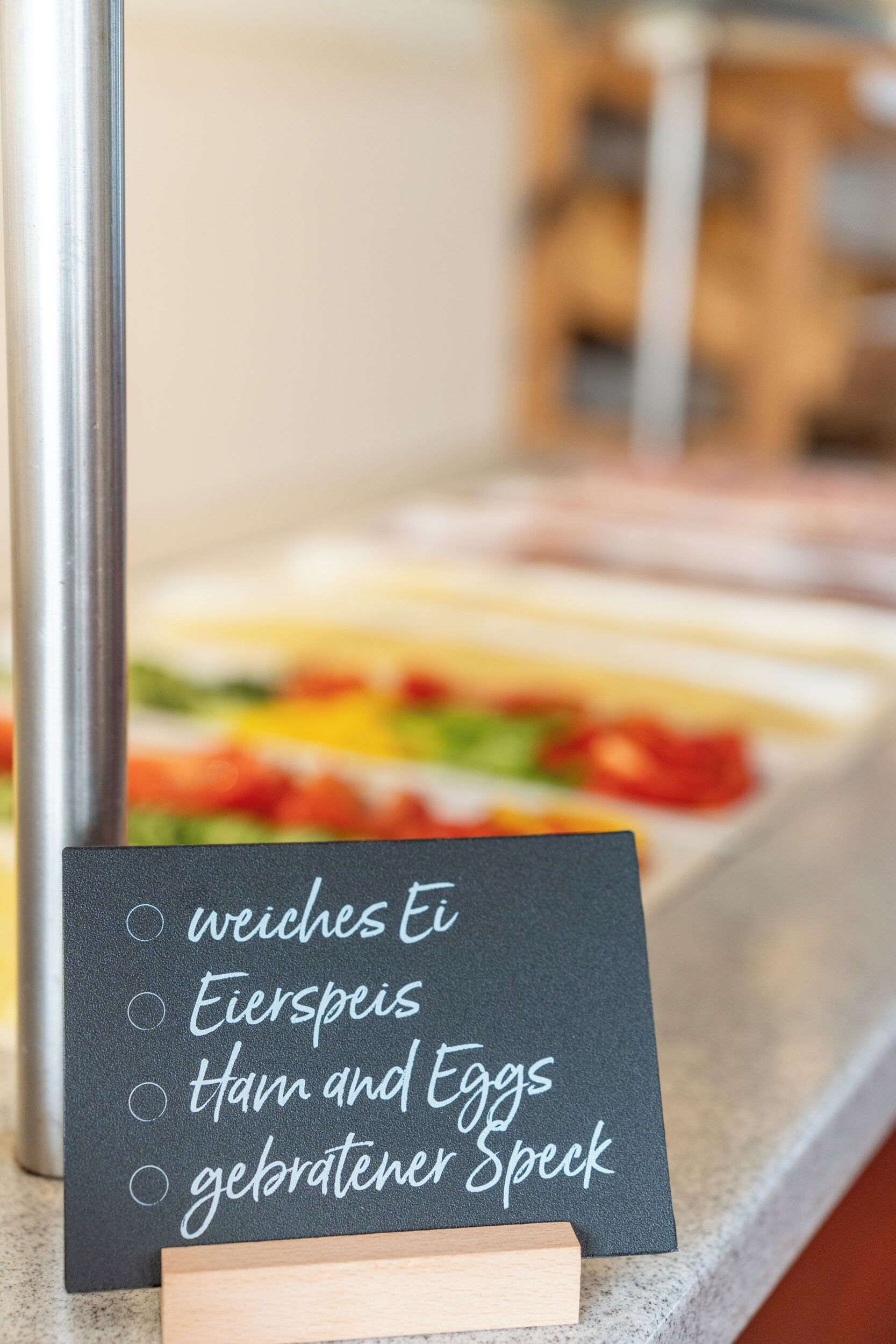 Quadro de menu com opções de café da manhã, incluindo 'Weiches Ei', 'Eierspeis', 'Ovos com Presunto' e 'Bacon Frito'.