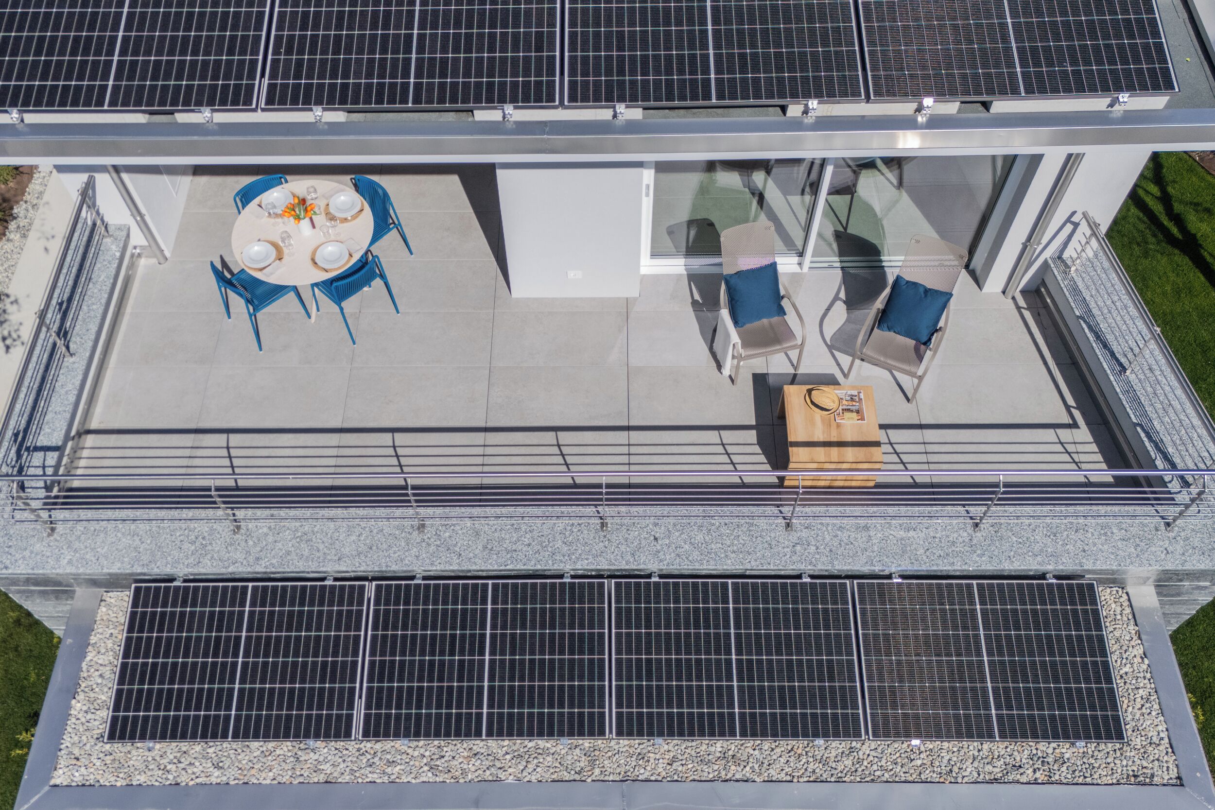 Terraço no telhado com painéis solares, mesa de jantar com cadeiras e área de estar com uma poltrona e uma mesinha.