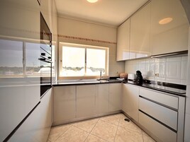 Uma cozinha moderna com armários brancos, bancada preta e janela com vista para o exterior.