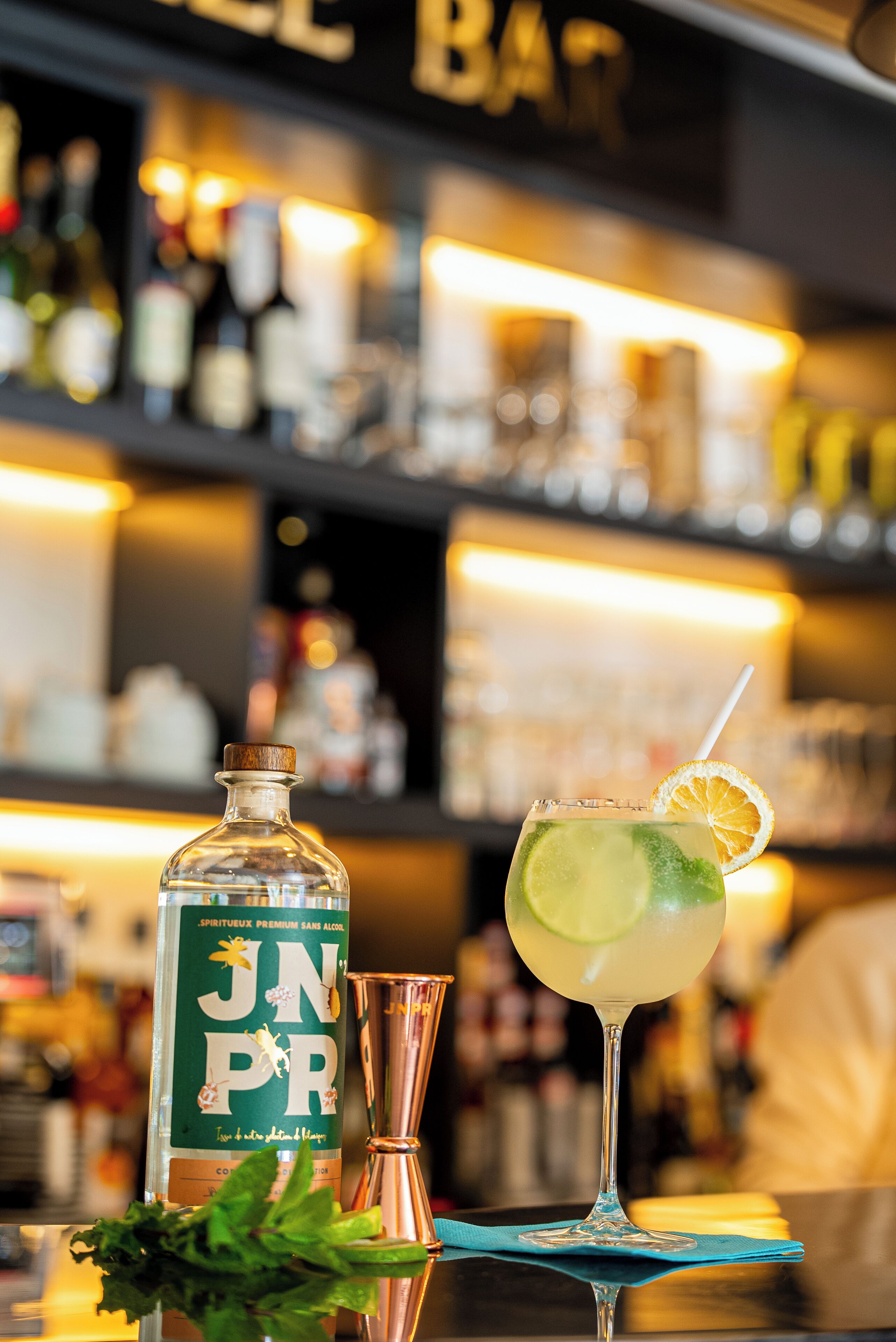 Um bar com uma garrafa de J&NPR, um copo de coquetel com uma fatia de limão e um coqueteleira de cobre.