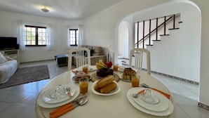 Uma área de refeições com uma mesa posta para o café da manhã, um sofá e uma escada.