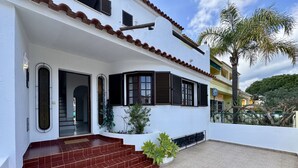 Um edifício branco com degraus de telha vermelha, persianas pretas e uma palmeira.
