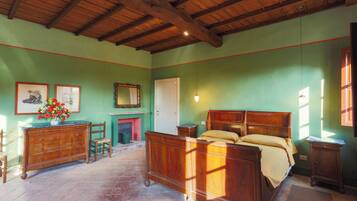Quarto com cama de madeira, penteadeira, cadeira, lareira e quadros nas paredes.