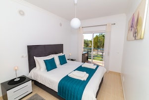 Quarto com cama, mesa de cabeceira e vista para uma varanda.