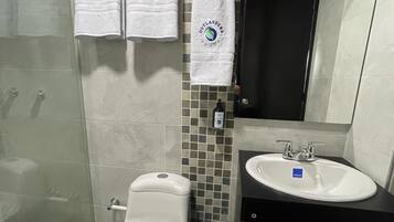 Casa de banho com sanita, lavatório e cabine de duche em vidro. Há duas toalhas penduradas na parede.