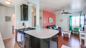 Cozinha moderna com ilha central, sala de jantar com mesa branca e sala de estar com sofá e decoração de estrela-do-mar.