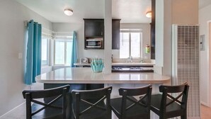 Uma cozinha moderna com ilha central, armários escuros, micro-ondas e janela com cortinas.
