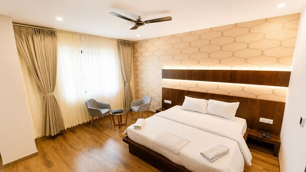 Quarto de hotel com uma cama grande, duas cadeiras, um ventilador de teto e parede com padrão.