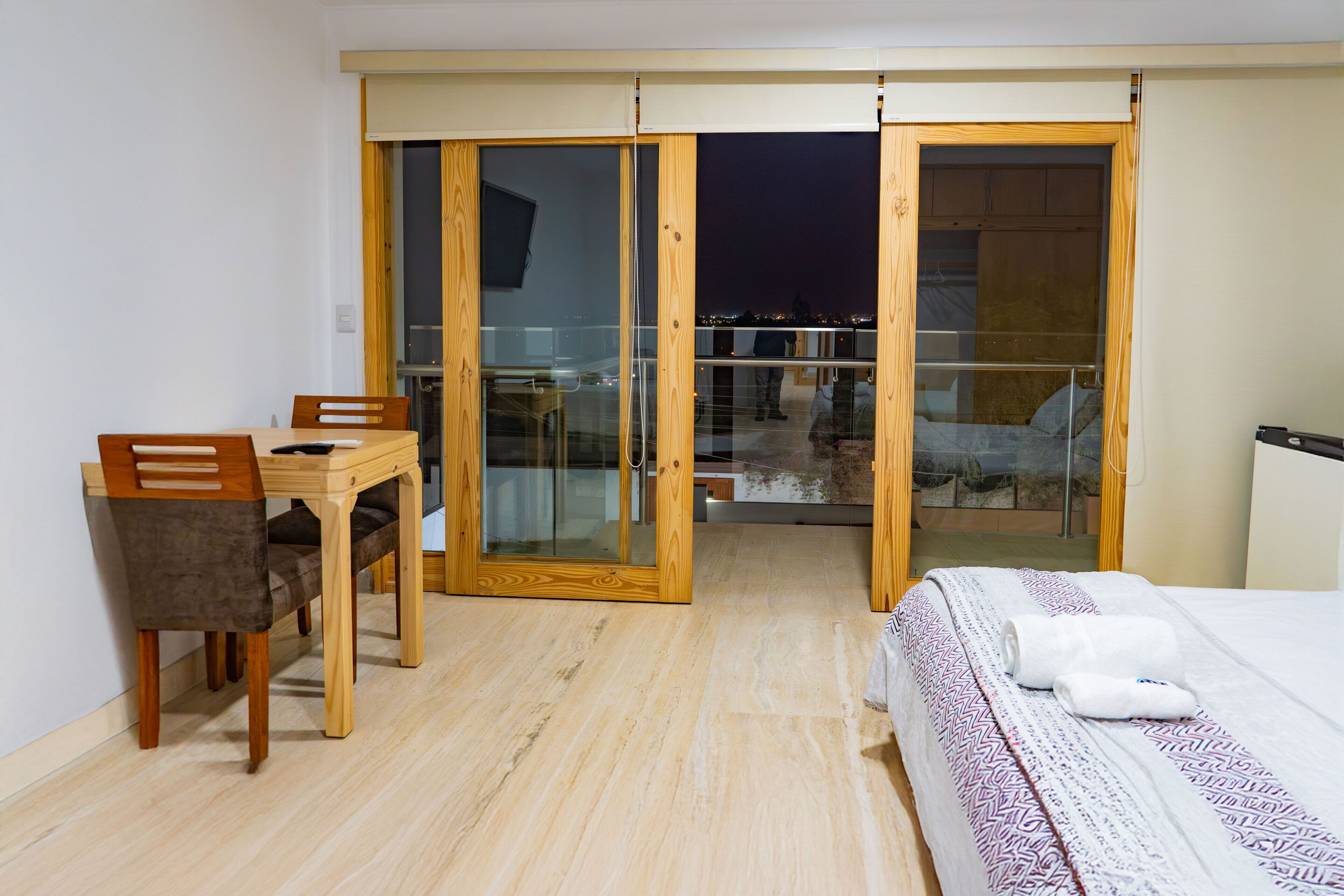 Quarto com uma cama, uma escrivaninha com cadeira e uma porta de vidro deslizante para uma varanda externa.