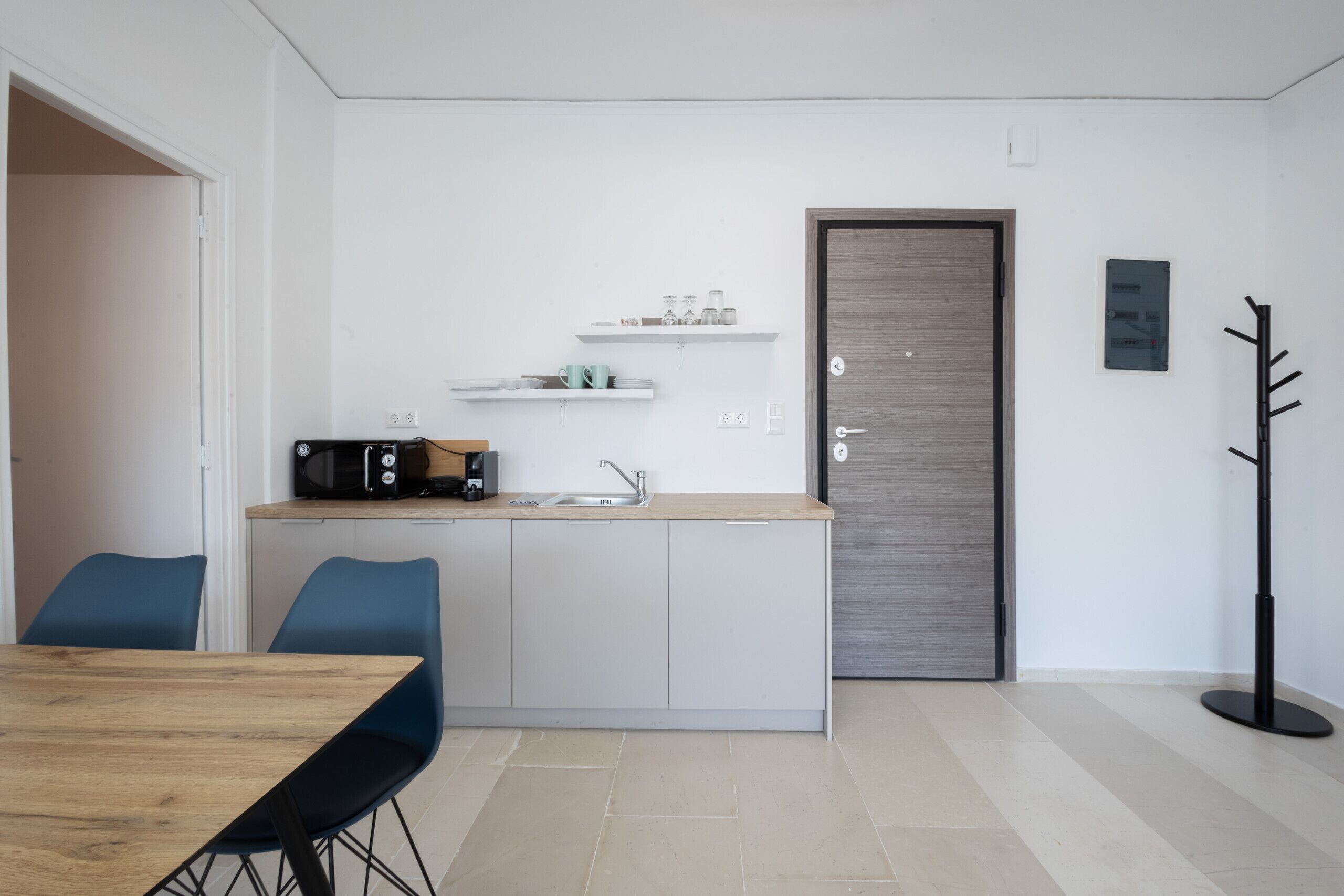 Cozinha moderna com bancada de madeira, pia embutida e micro-ondas. Há duas cadeiras azuis e uma mesa de jantar de madeira. Um porta-roupas está visível à direita.