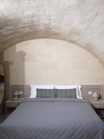Quarto com cama, duas mesas de cabeceira e teto de pedra em arco.