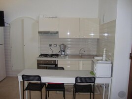 Uma cozinha compacta com armários brancos, fogão a gás, micro-ondas e duas cadeiras pretas.
