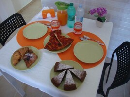 Uma mesa de café da manhã com pratos de comida, um croissant, uma fatia de pizza e um copo de suco de laranja.