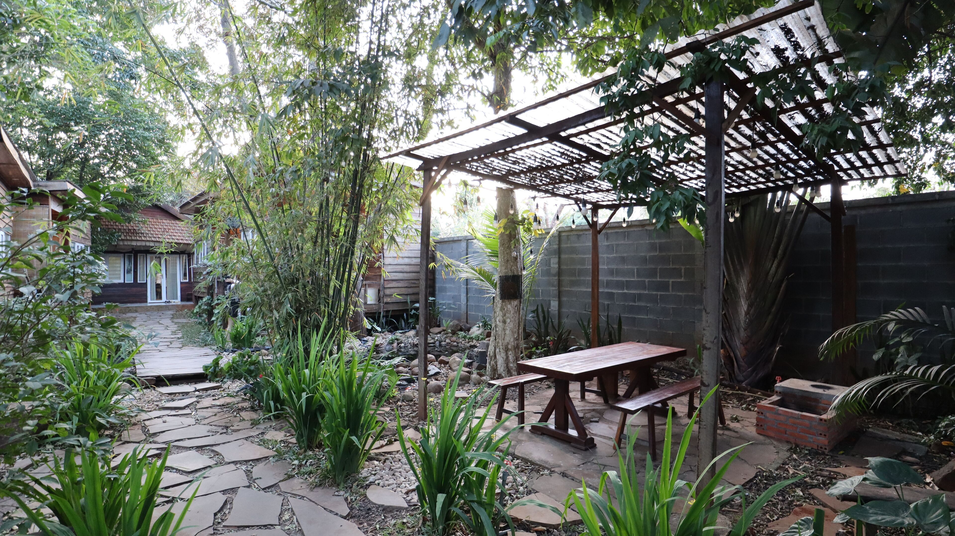 Uma área de pátio com pérgola, caminho de pedra e mesa de madeira.