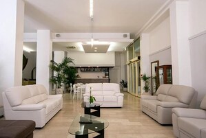 Uma sala de estar ampla com um conjunto de sofá branco, uma mesa de centro de vidro e uma área de cozinha ao fundo.