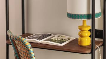 Uma cadeira de vime com assento e encosto trançados, uma mesa de madeira com um abajur amarelo e um livro aberto sobre a mesa.