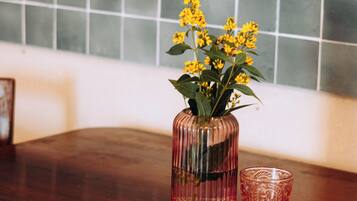 Uma mesa de madeira com um vaso de vidro contendo flores amarelas e um copo ao lado.