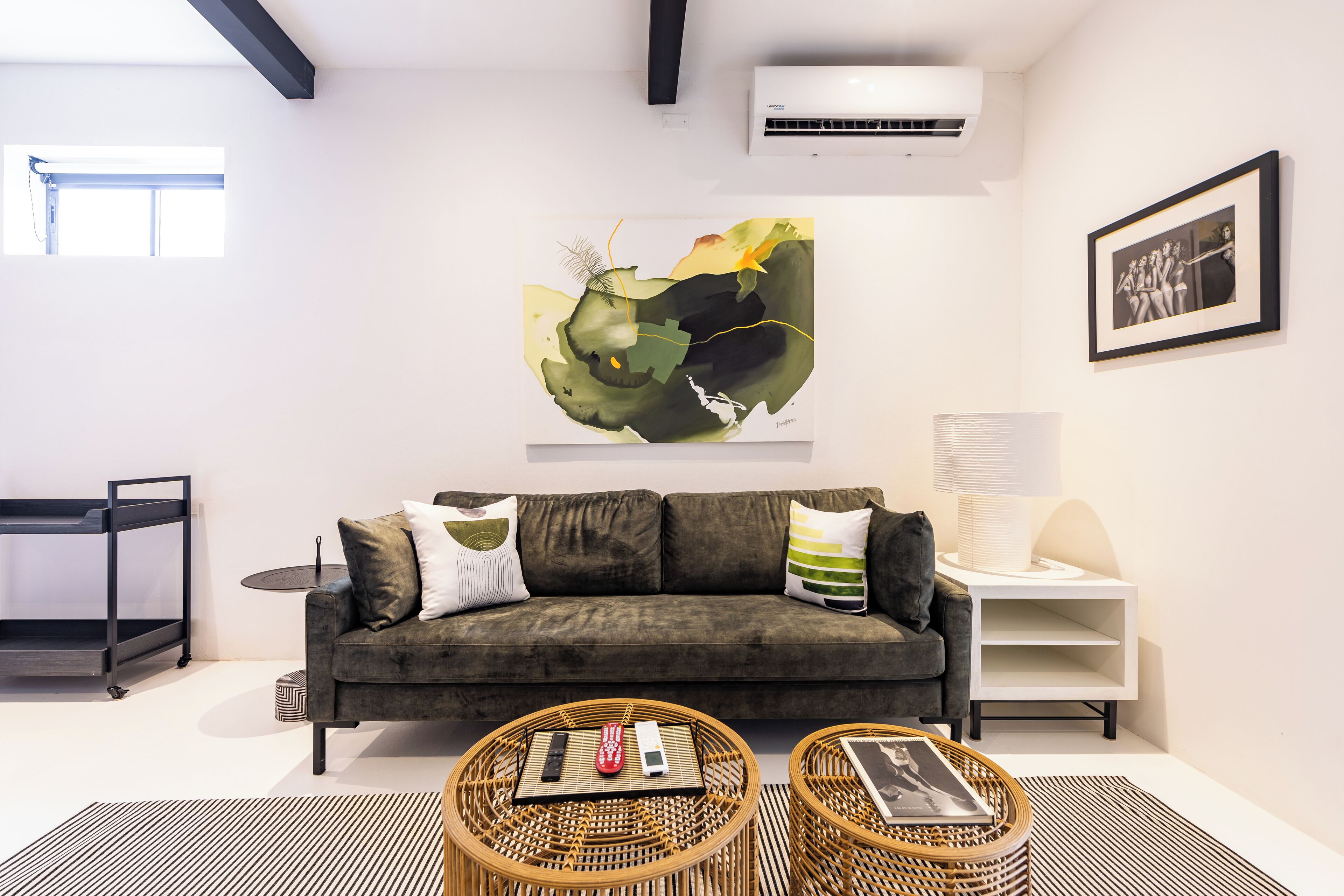 Uma sala de estar moderna com um sofá cinza escuro, duas mesas laterais de vime, uma pintura abstrata grande e uma fotografia emoldurada na parede.