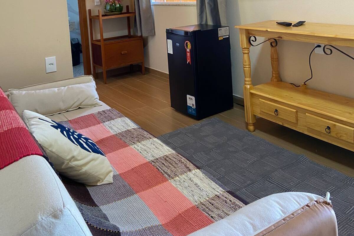 Um quarto aconchegante com uma cama, uma TV, um pequeno frigorífico e uma escrivaninha de madeira.