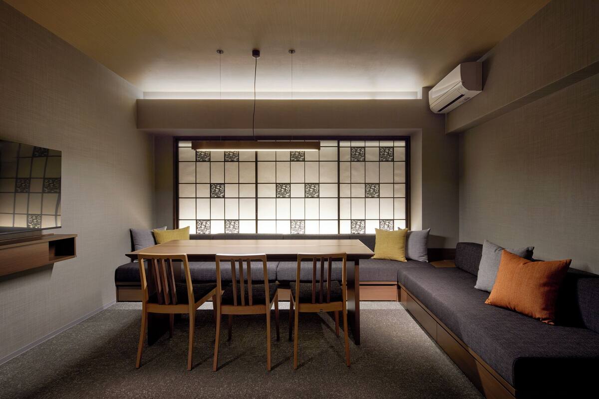 Um interior moderno com mesa de jantar, cadeiras, sofá e uma janela grande com um painel decorativo.