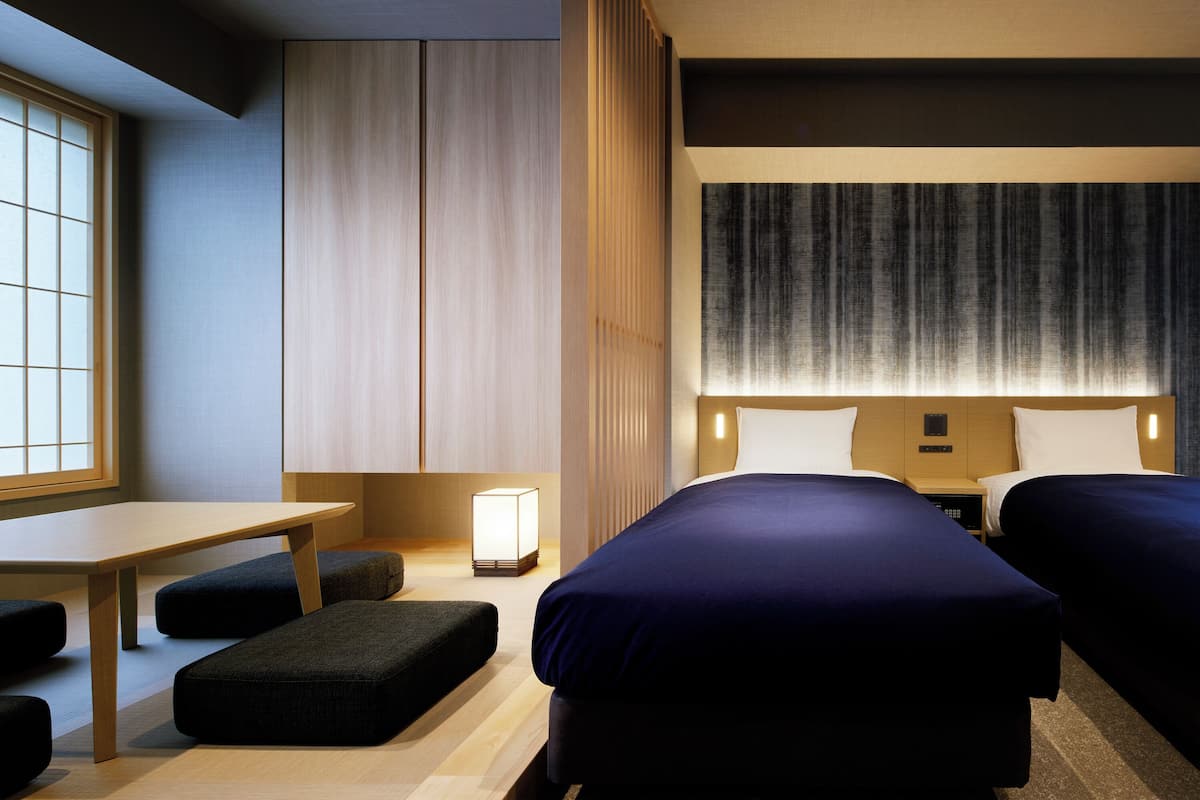 Quarto de hotel com duas camas, uma escrivaninha e um espaço para sentar.