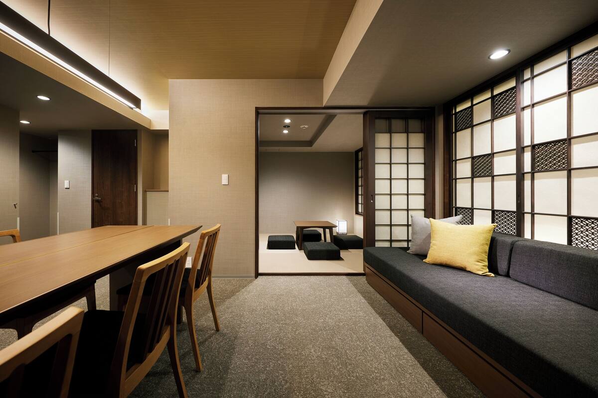 Quarto moderno com mesa de jantar de madeira, cadeiras, sofá com almofadas e um painel deslizante shoji.