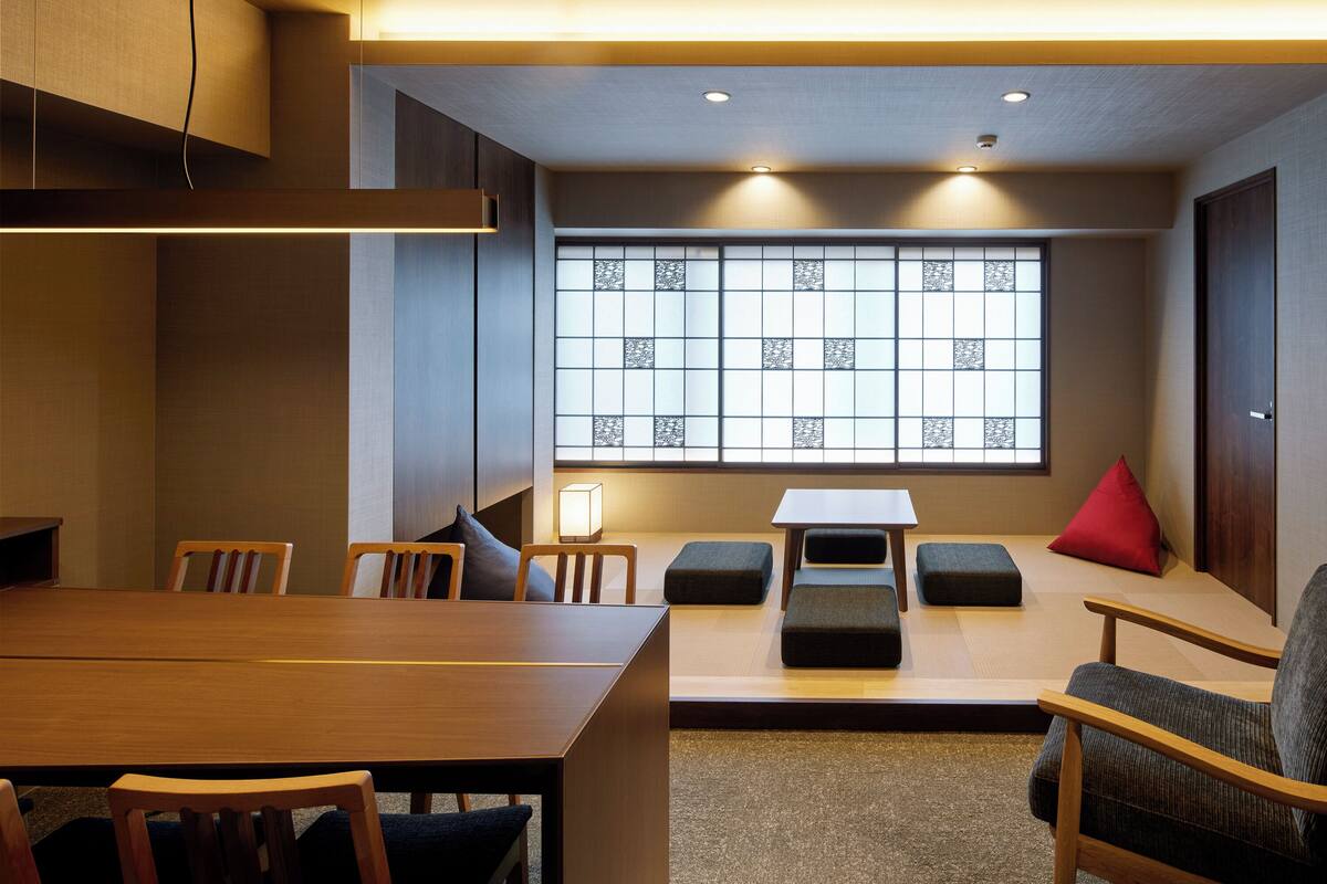 Um interior moderno com mesa de jantar de madeira, assentos acolchoados e uma grande janela com painéis de vidro decorativos.