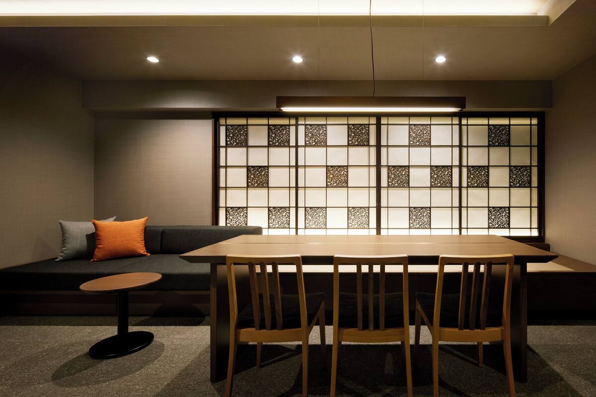 Uma área de refeições moderna com mesa e cadeiras de madeira, uma mesinha redonda e um sofá com almofadas.