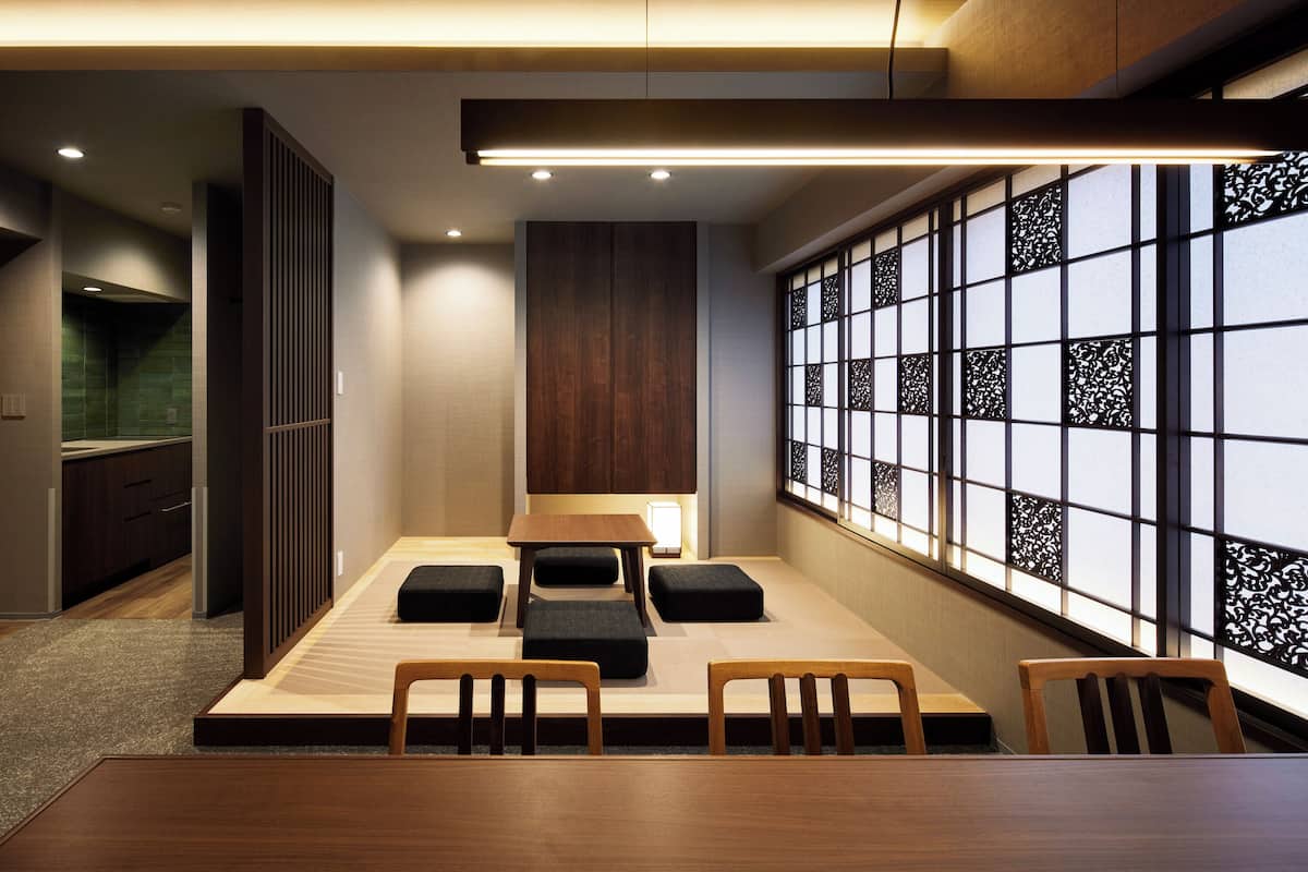 Uma área de refeições moderna com mesa de madeira, assentos acolchoados pretos e uma parede divisória decorativa.