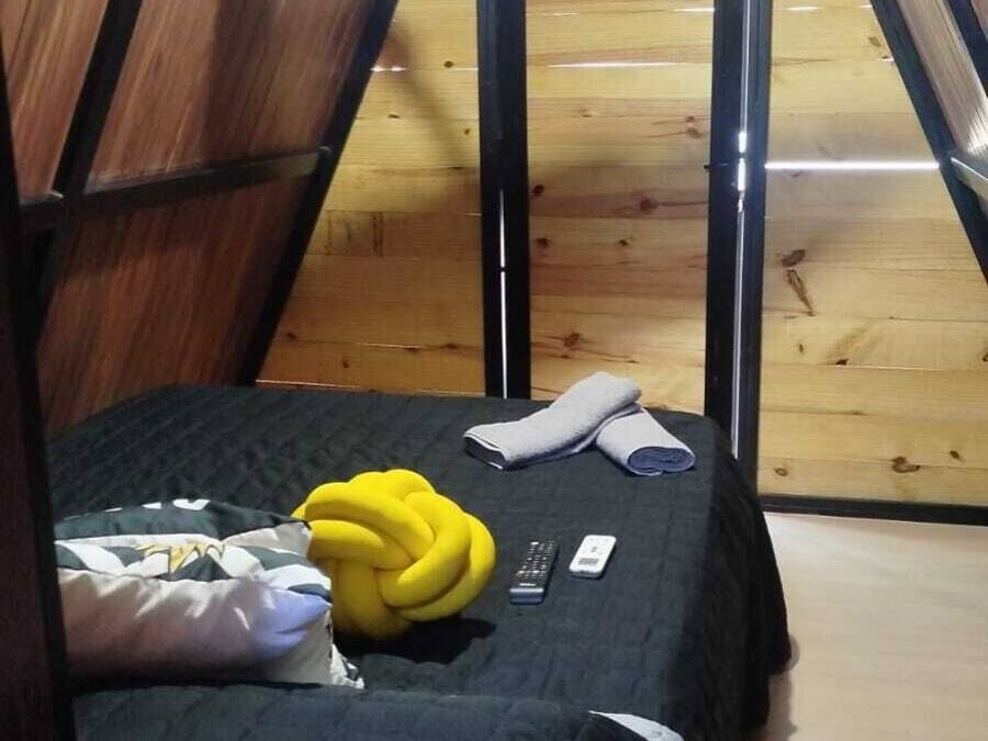 Quarto com cama, televisão fixada na parede e teto inclinado de madeira.