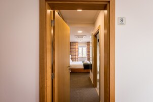 Corredor de hotel que leva a um quarto com cama, janela com cortinas e placa indicando o número 8.