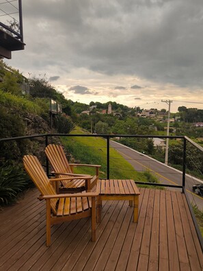 Um deck de madeira com duas cadeiras Adirondack com vista para uma estrada e uma cidade.
