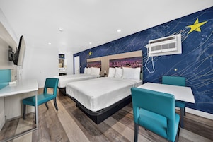 Quarto de hotel com uma cama, duas cadeiras, uma escrivaninha e uma parede com um desenho de noite estrelada.