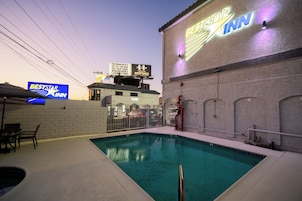 Uma área de piscina com uma placa da BestStar Inn, uma área de estar coberta e um edifício com uma grande placa iluminada da BestStar Inn.