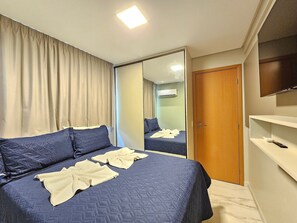 Quarto de hotel com cama, espelho, guarda-roupa e televisão.